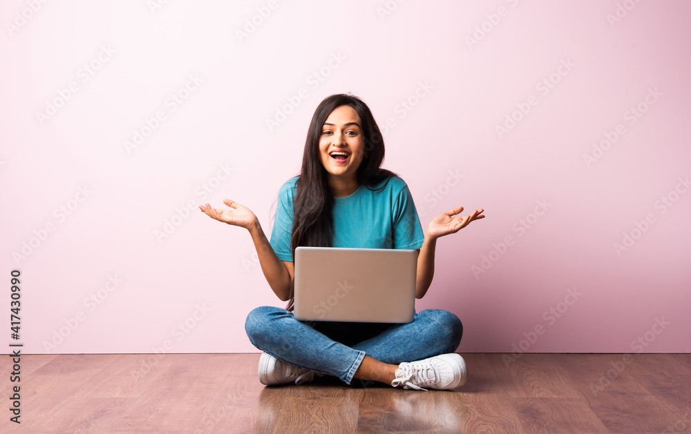 Indian asian girl using laptop while sitting against pink wall on ...