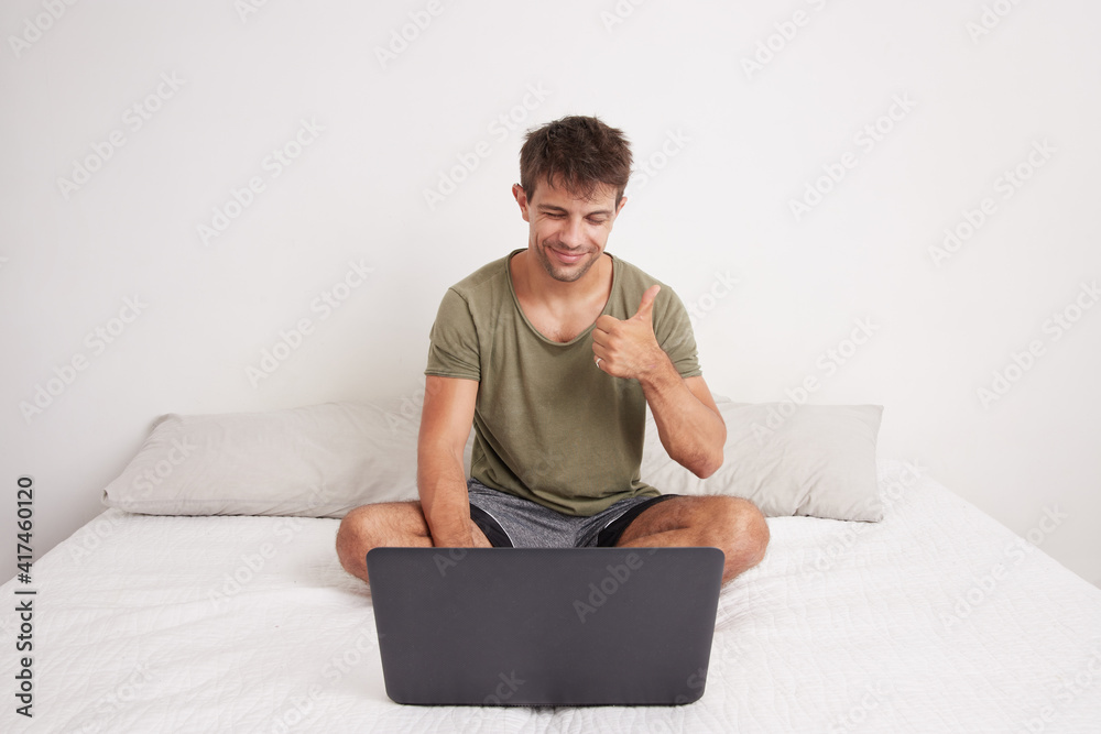 Young man sitting on his bed on video call with his laptop computer ...