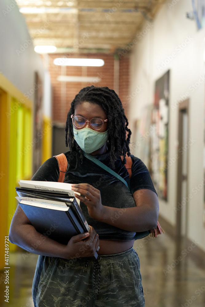 Black female college student walking down hallway with school books ...