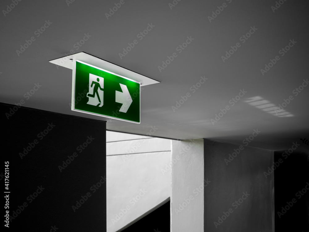 Green emergency exit sign hanging from ceiling. Stock Photo | Adobe Stock