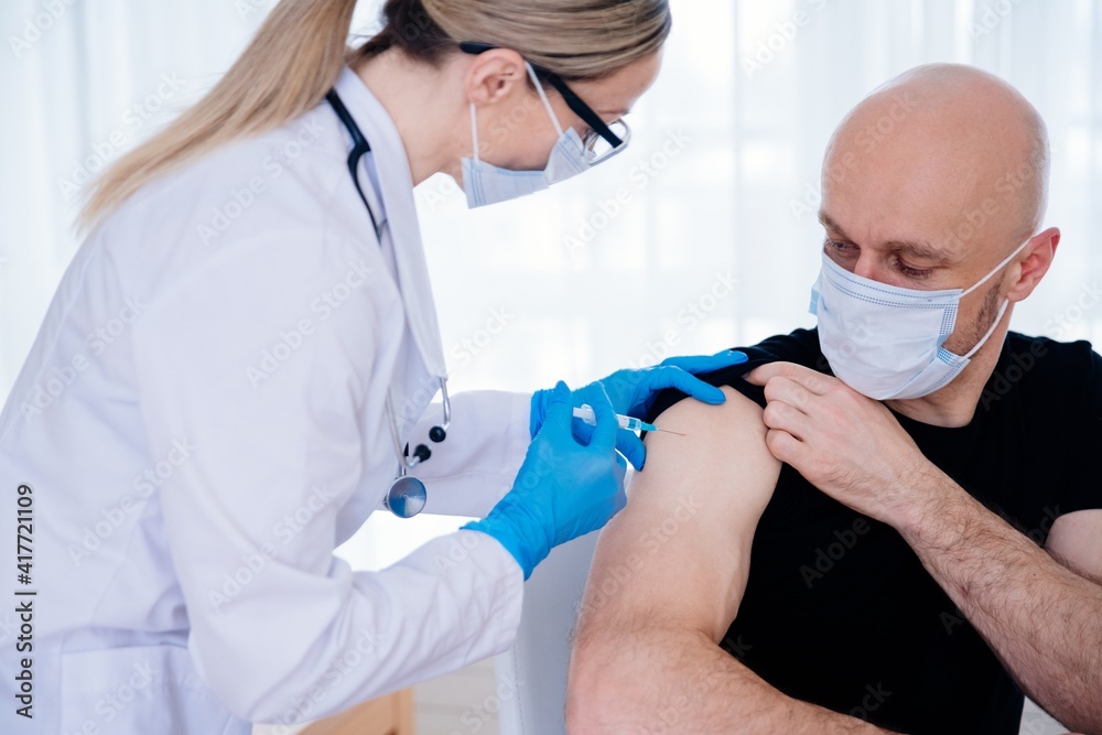 Female doctor injects the vaccine into the arm of a male patient ...
