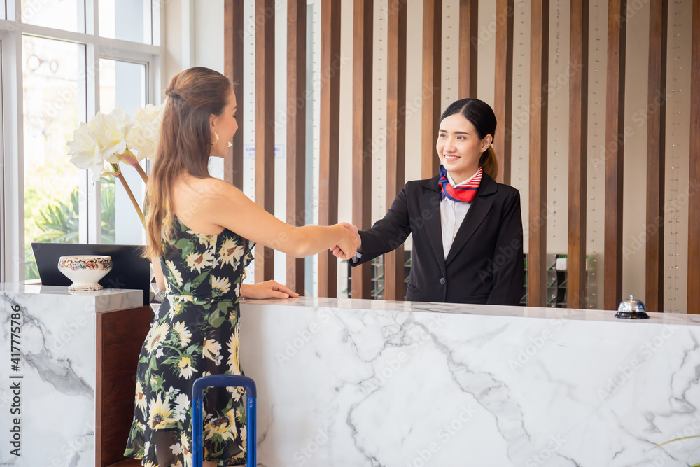 Happy receptionist and guest making handshake at hotel reception ...