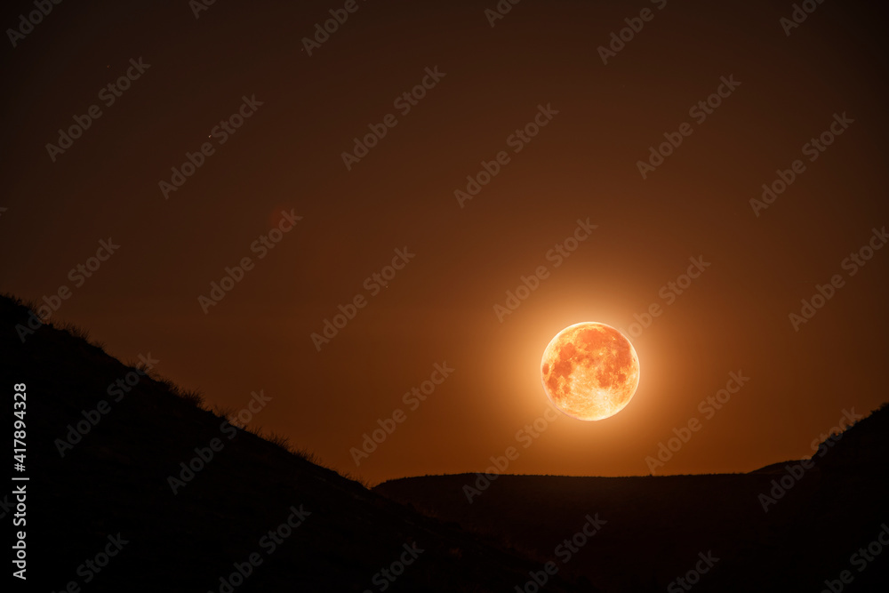 Amazing full red moon in the night sky illuminates hills silhouette ...