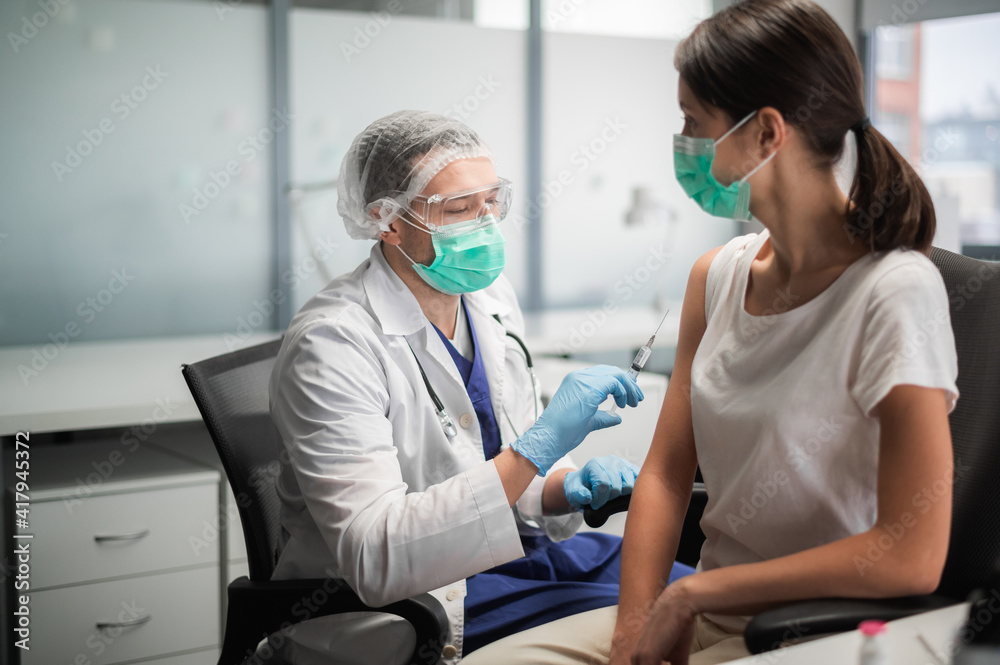 An experienced doctor in a mask does the vaccination in his office in a ...
