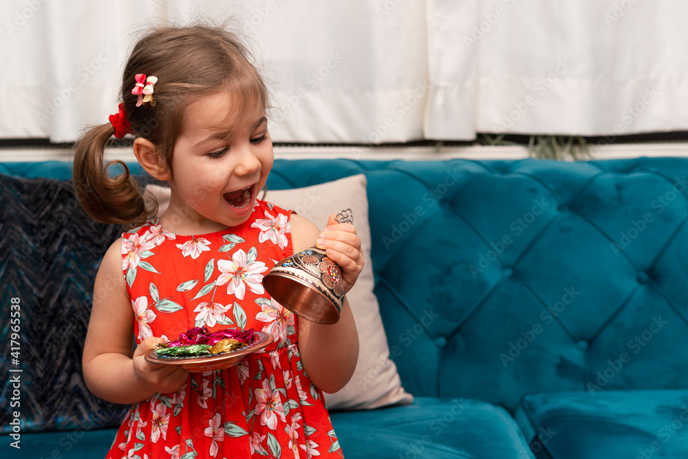 Portrait of cute baby girl holding candies from during Ramadan feast ...