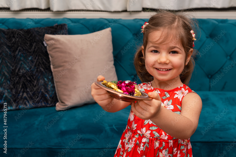 Portrait of cute baby girl holding candies from during Ramadan feast ...