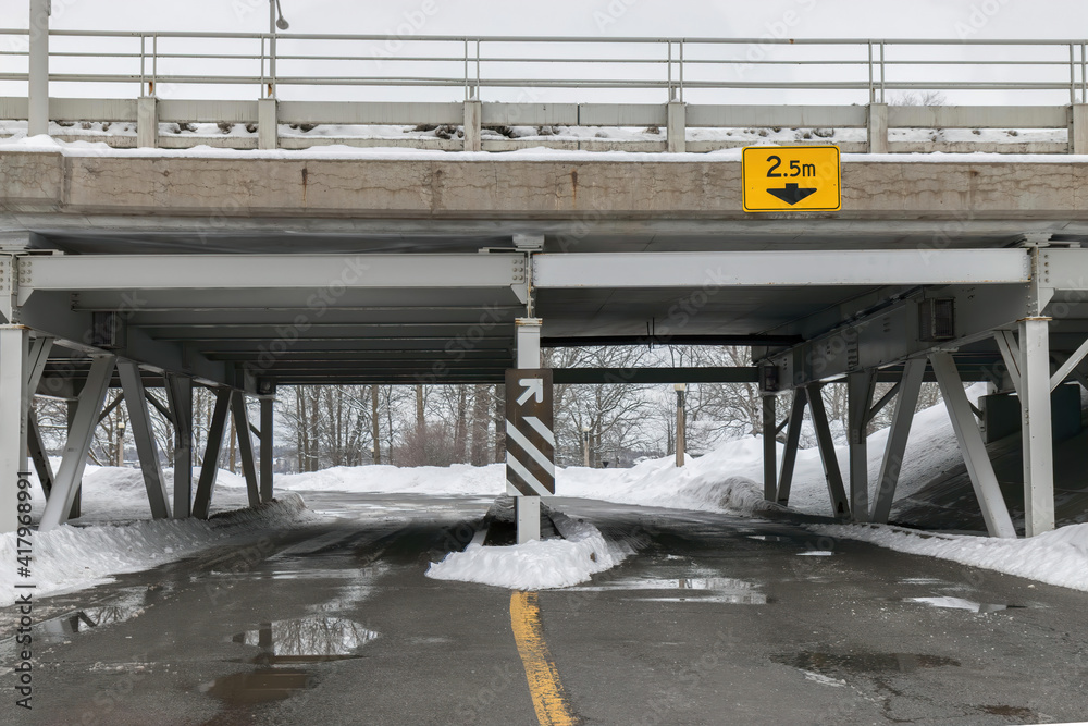 Paved roadway under a low concrete bridge deck in winter with ...
