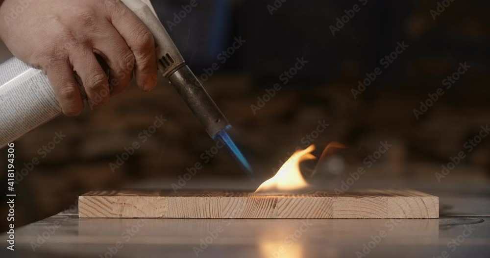 Craftsman carpenter scorches a wooden board with a gas-burner in slow ...