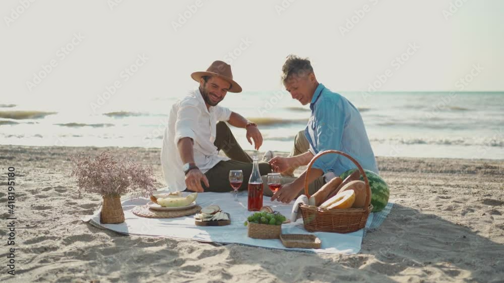 Lgbt gay couple having romantic picnic at the beach, holding hand each ...