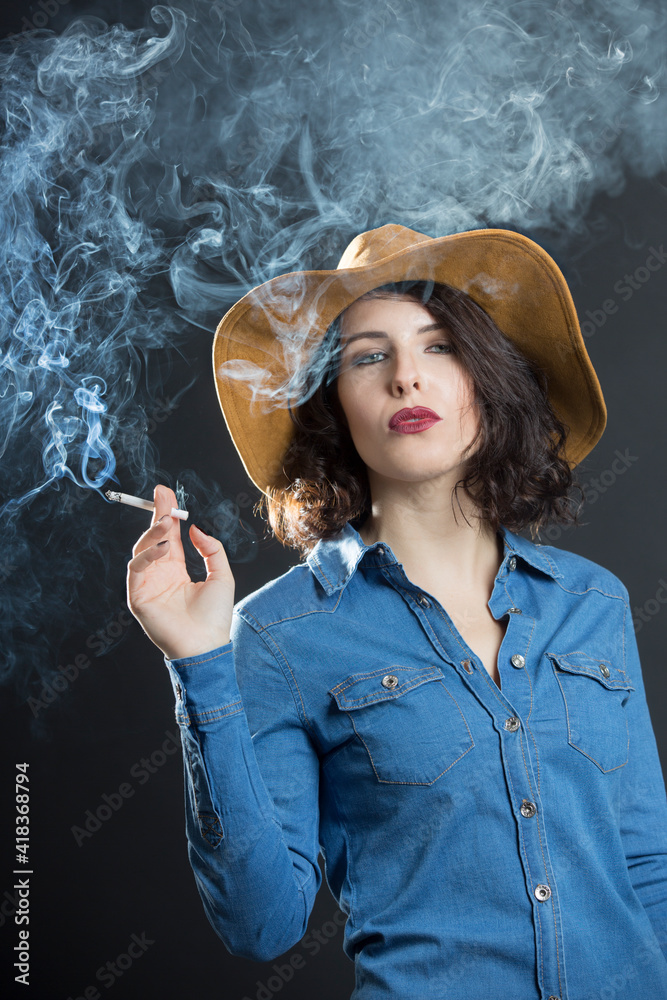 ragazza mora con camicia in jeans e cappello da cowboy, fuma una sigaretta producendo moltissimo ...