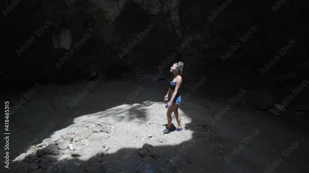 An attractive young woman in a large cave walks into a large patch of ...