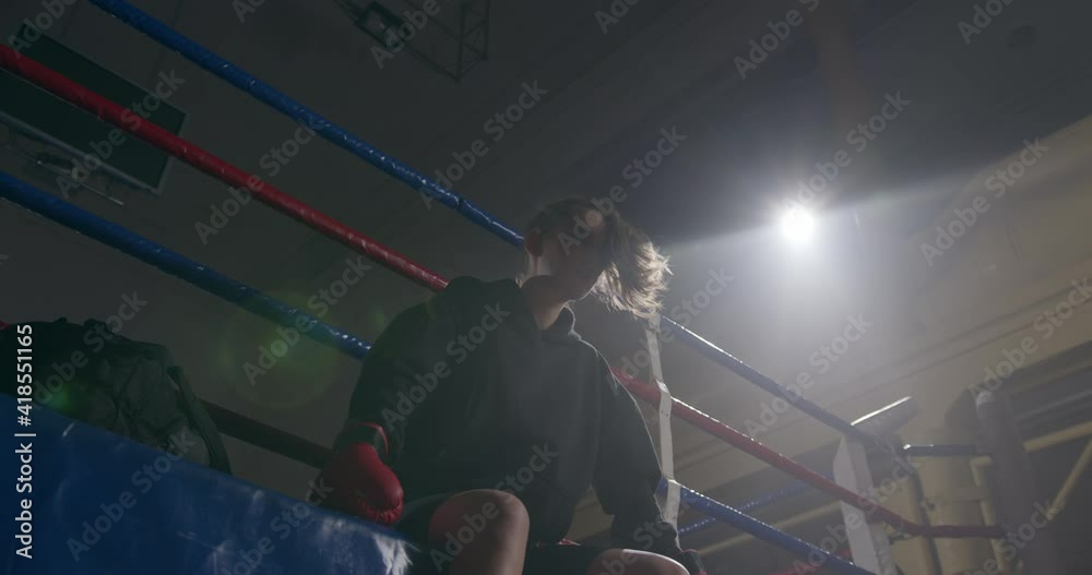 Tired female boxer sitting on boxing ring after kickboxing workout in ...