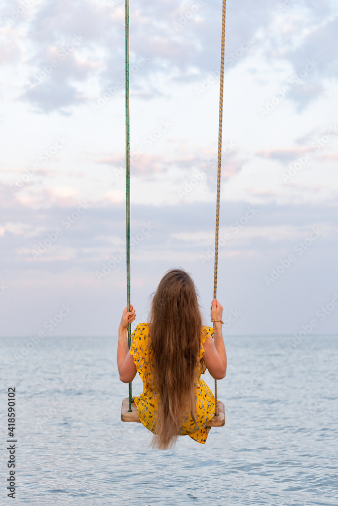 Girl with beautiful long hair sits on swing on sea background. Back ...