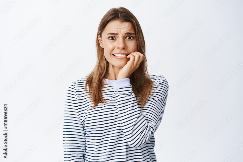 Scared blond girl biting nails on fingers and frowning, afraid of ...