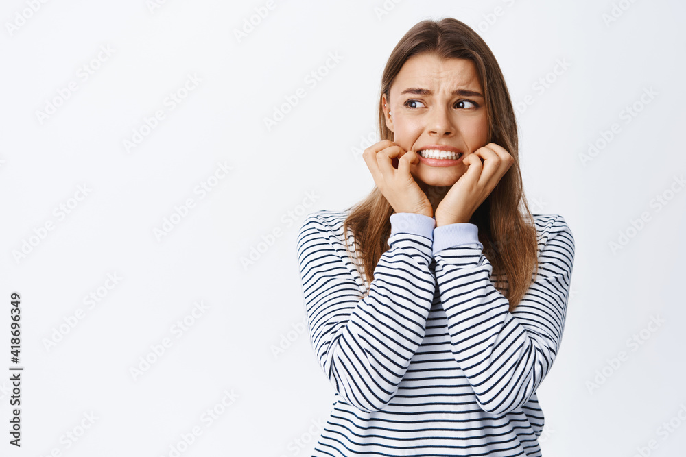 Scared blond girl panicking, biting fingernails and looking left at ...