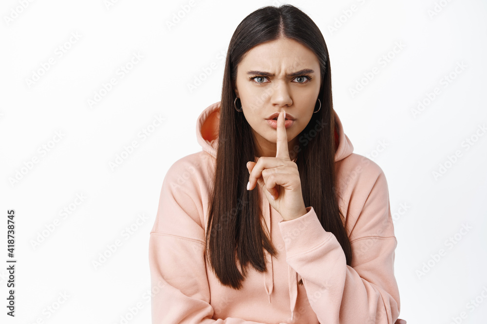 Portrait of angry and bossy young woman frowning, shushing at camera ...