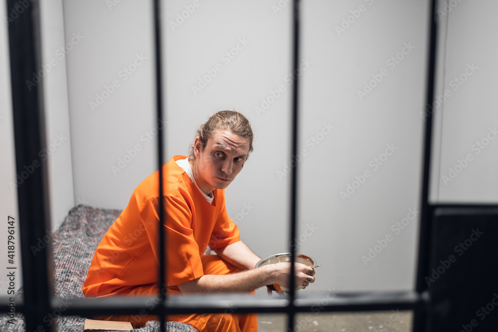 A high-security prison inmate in a red prison uniform eats from an iron ...