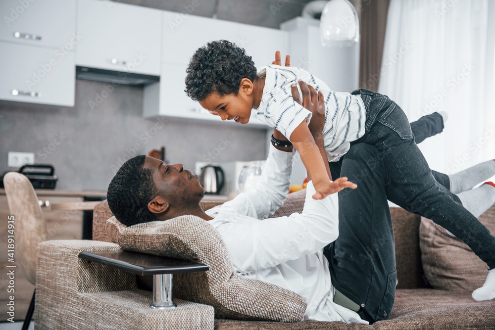 African american father with his son is indoors at home lying on the ...