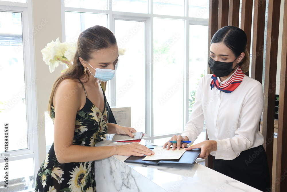 A tourist woman and receptionist at counter in hotel wearing medical ...