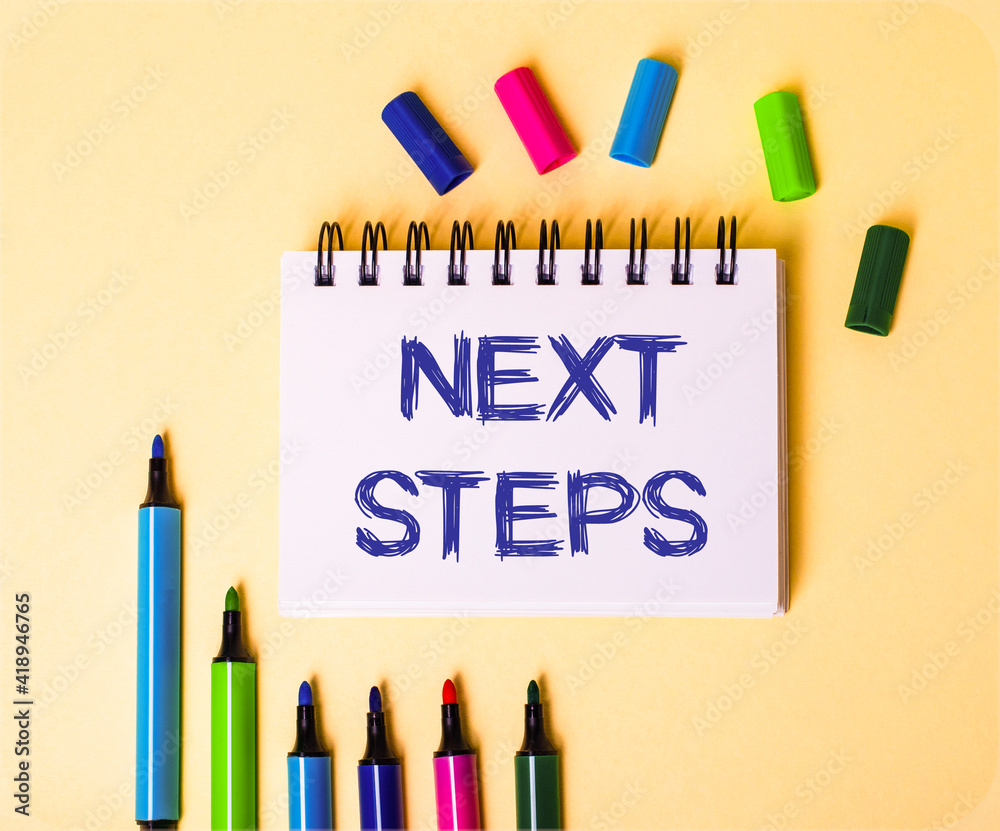 The words NEXT STEPS written in a white notebook on a beige background ...