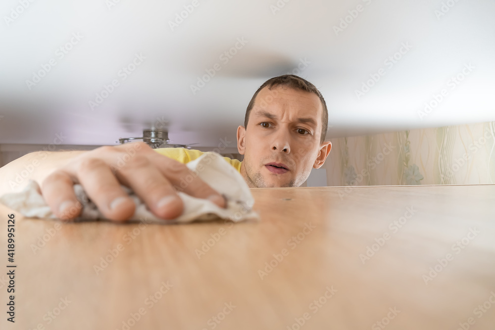 Concept of cleaning the house. a man wipes dust from a tall cabinet in ...