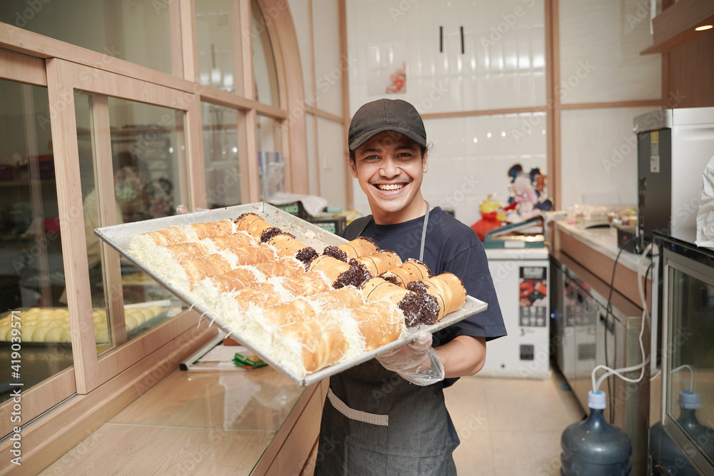 handsome asian smiling worker at the bakery shop holding a tray of ...