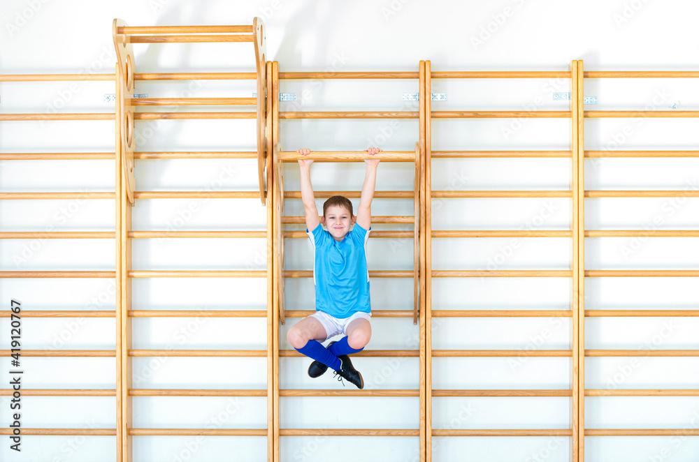 Kid at physical education lesson in school gym. Boy in gym doing pull ...