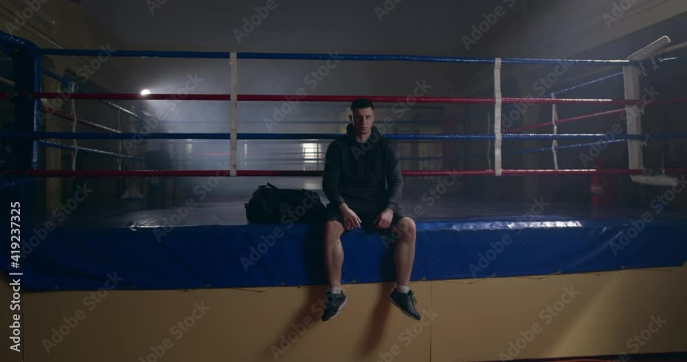 Devastated male boxer resting on empty boxing ring thinking of failure ...