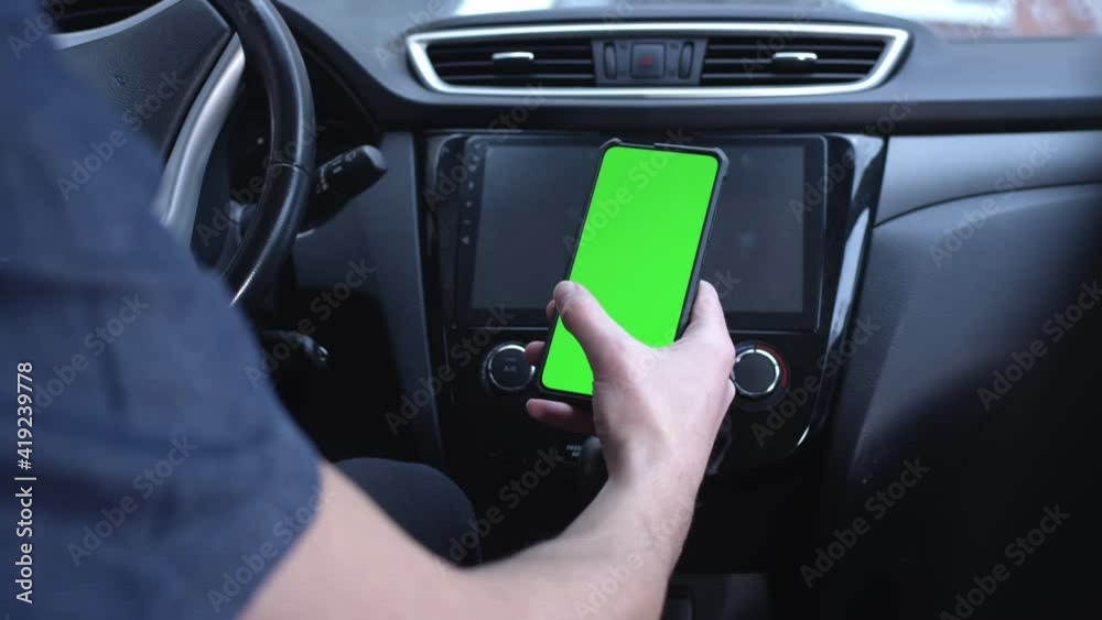 A male driver uses a smartphone vertically with a green screen, holds a ...