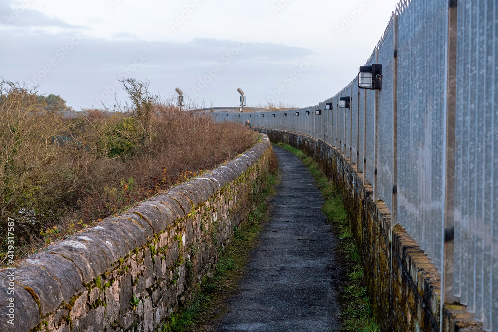 Metal fence with lights and narrow walk path. Perimeter of a safety ...