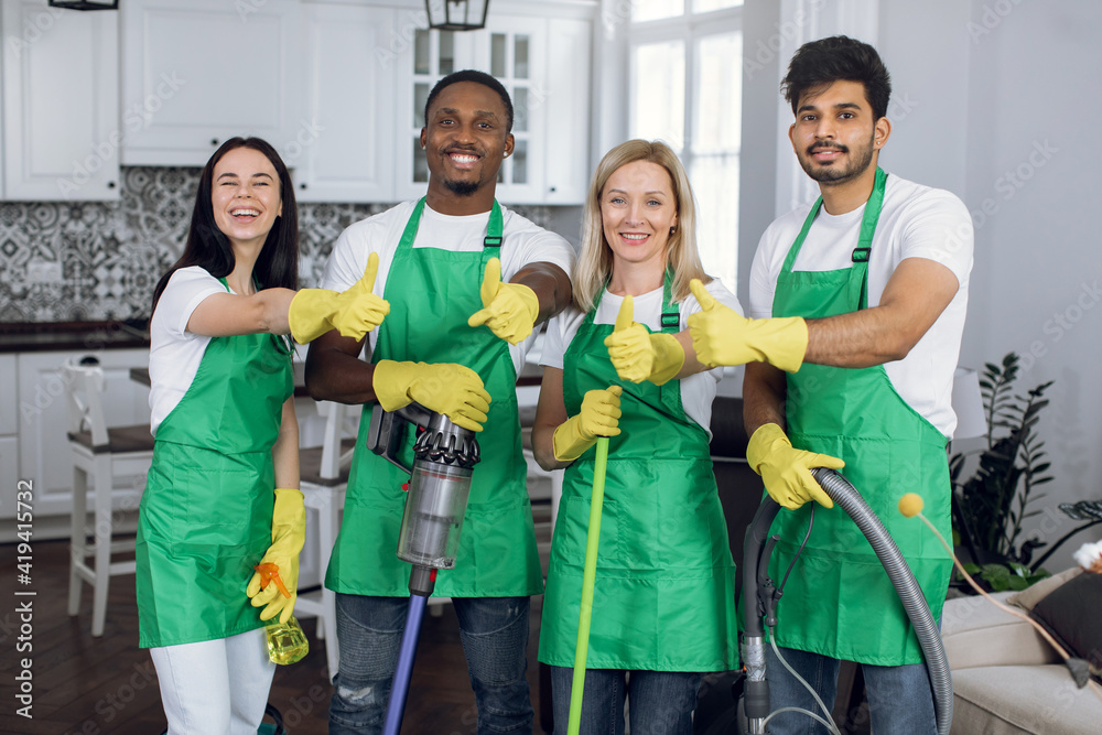 Smiling multiracial housekeepers in green aprons and yellow gloves ...