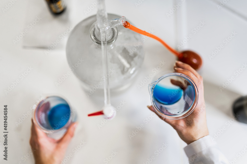From above of crop anonymous scientist with beaker with blue liquid in ...