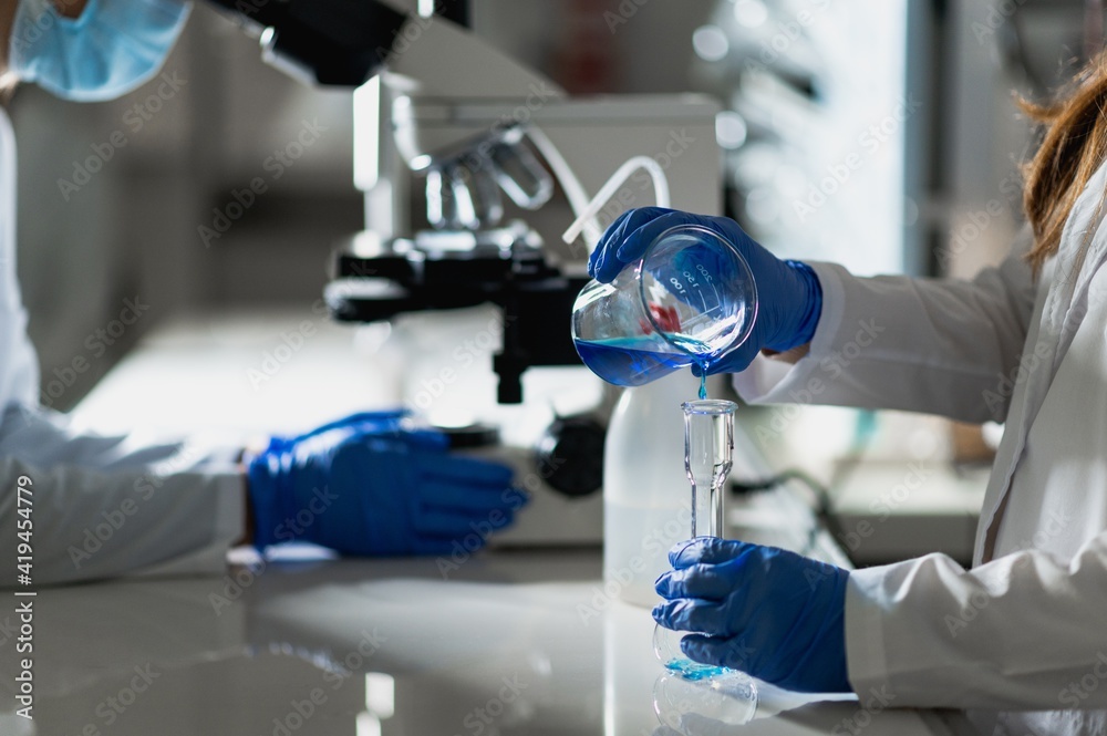Foto de Side view of crop unrecognizable female chemist pouring blue ...