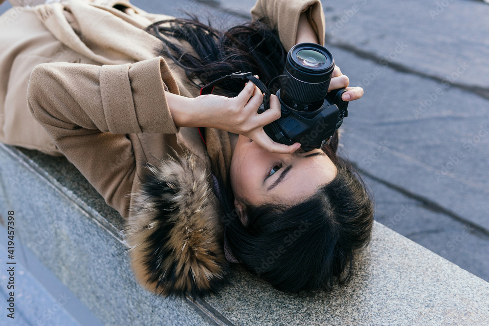 High angle of female photographer lying on stone parapet and shooting ...