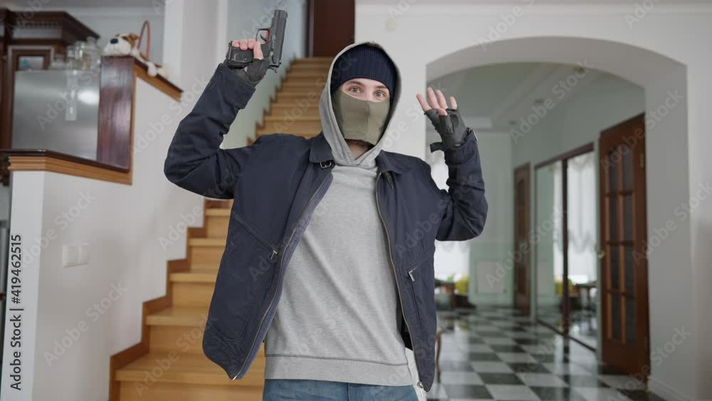 Middle shot of panicked young masked thief raising hands and looking at ...