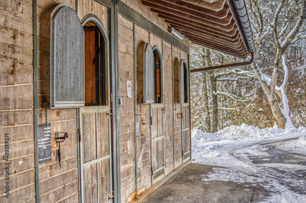 Focus on wooden horse stalls in winter. Snowy view at an outdoor horse ...