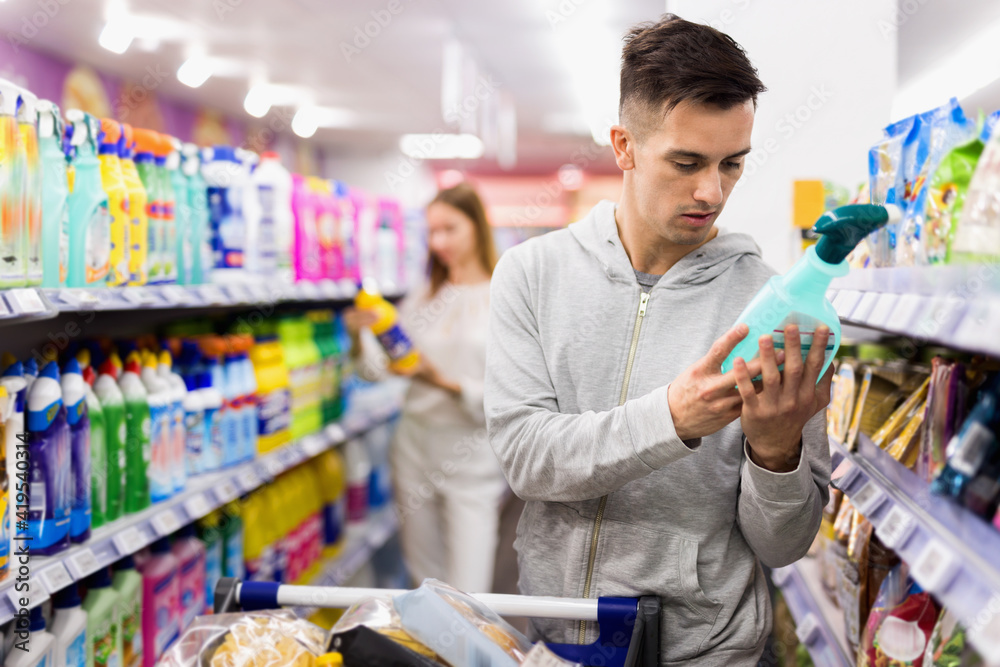 Young cheerful positive male customer making purchases in supermarket ...