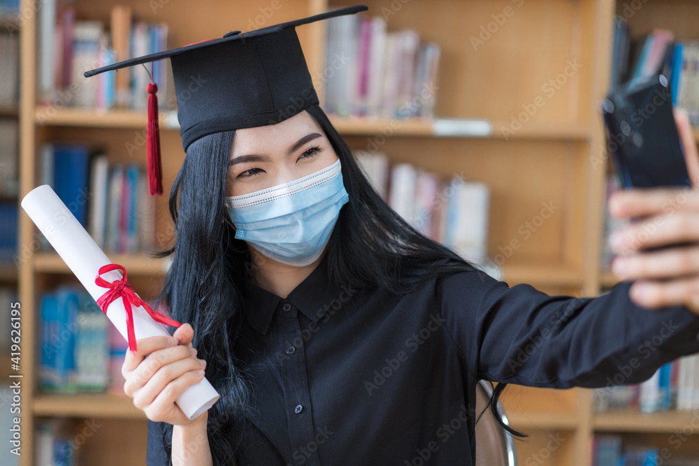 A young cheerful Asian woman university graduates in graduation gown ...