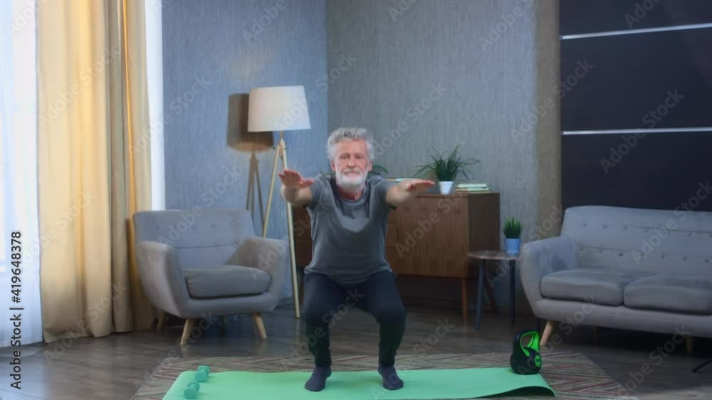 Portrait Of A Gray haired Senior Man With A Beard Squats Does Home Portrait Of A Gray haired Senior Man With A Beard Squats Does Home