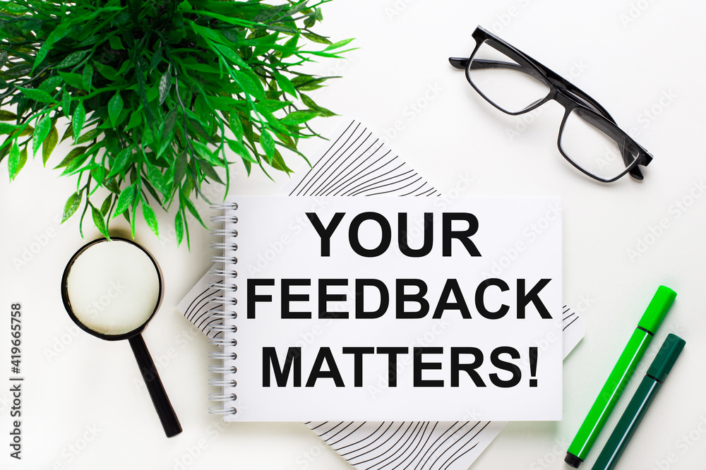 On a white background lies a notebook with words YOUR FEEDBACK MATTERS ...