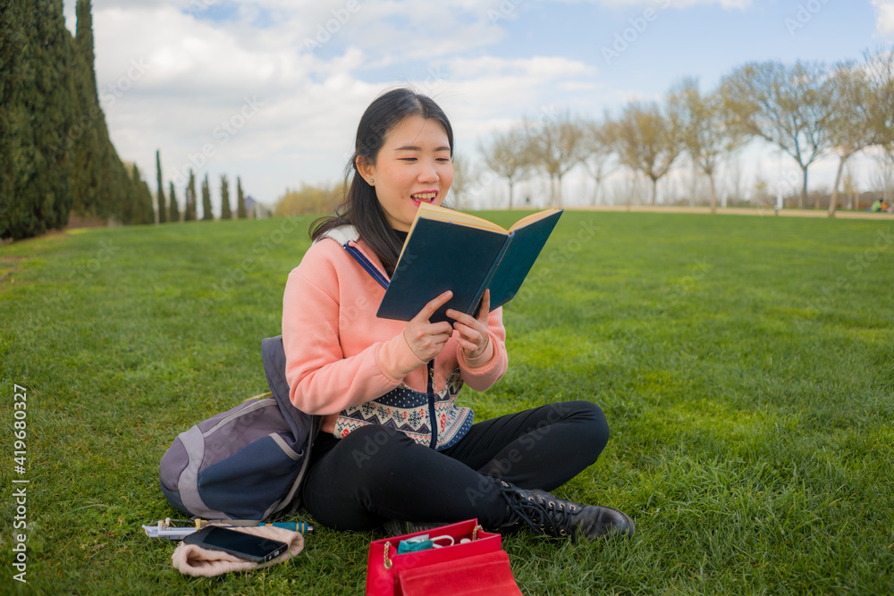 young Asian woman enjoying novel on grass - lifestyle portrait of young ...