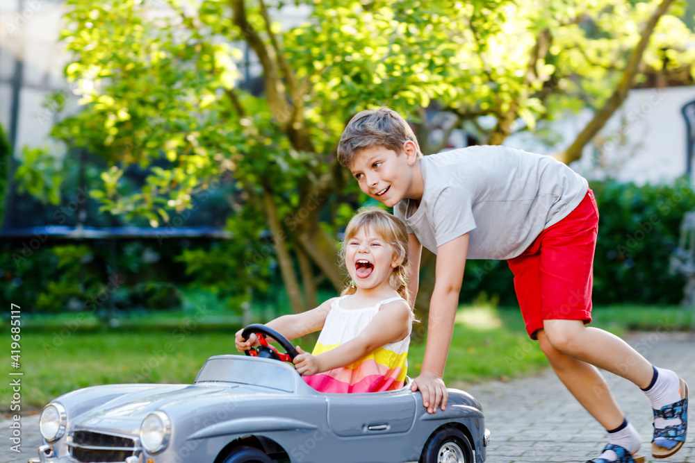 Two happy children playing with big old toy car in summer garden ...