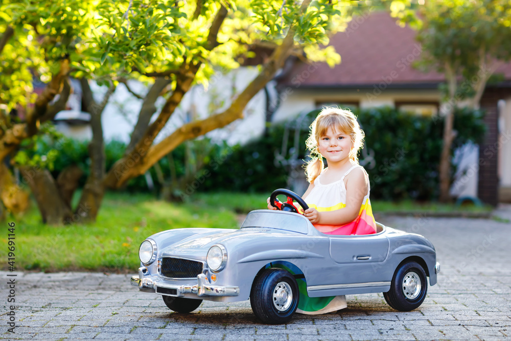 Little adorable toddler girl driving big vintage toy car and having fun ...