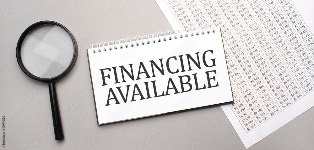 FINANCING AVAILABLE sign in white paper notepad and magnifying glass on ...