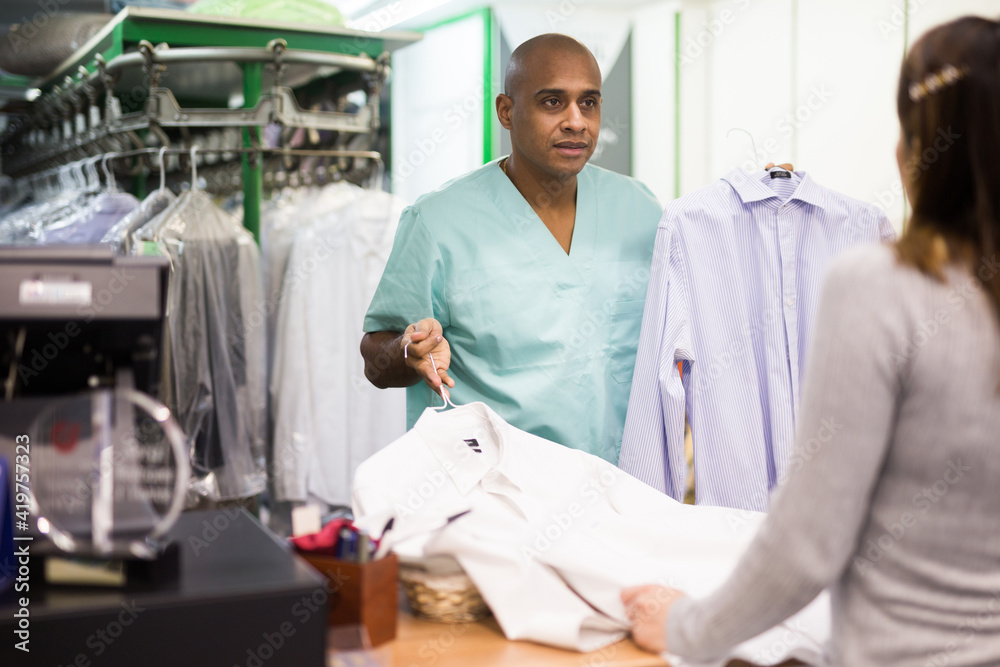 Positive man laundry worker returning clean clothes to customer at dry ...