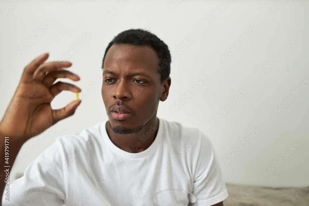 Handsome unshaven young dark skinned man holding yellow capsule of ...