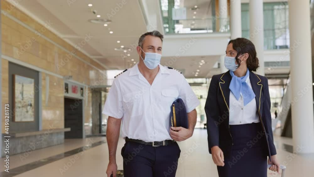 Airliner pilot and air hostess wearing face mask walking in airport ...