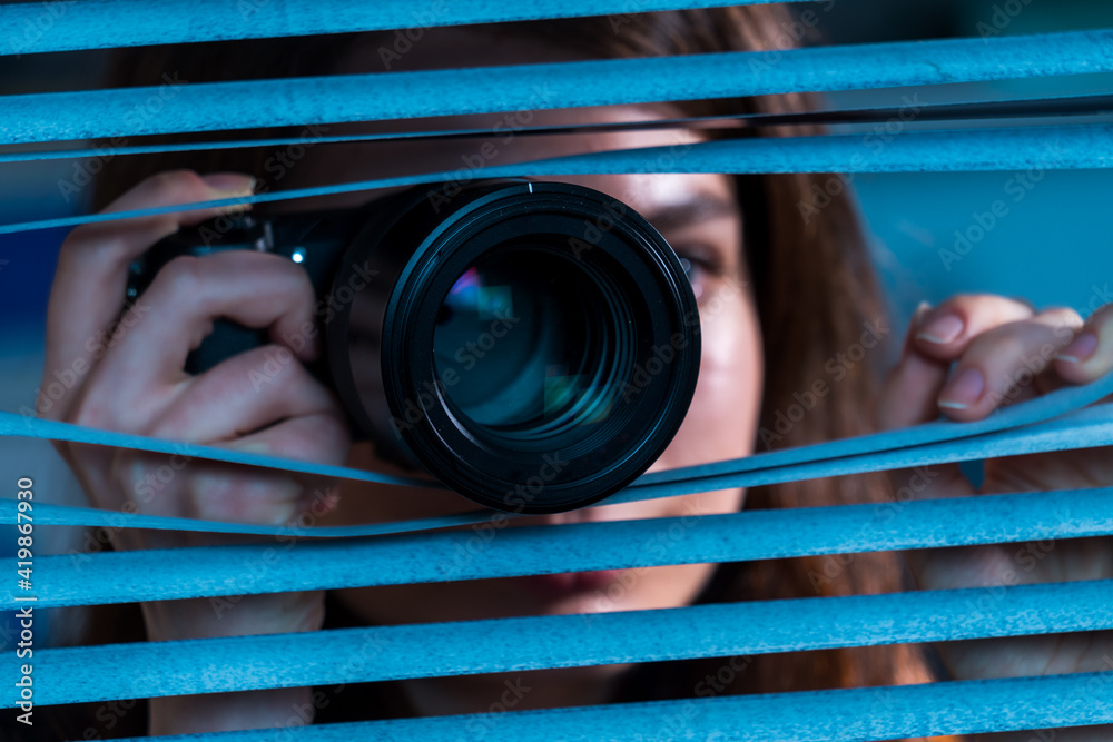 Young paparazzi woman with photo camera in hand looks out the window ...