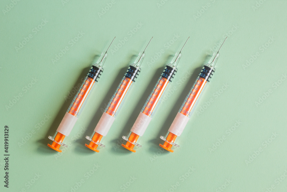 Four vaccination syringes with the needle uncapped forming a line ...