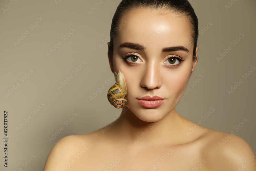 Beautiful young woman with snail on her face against beige background ...